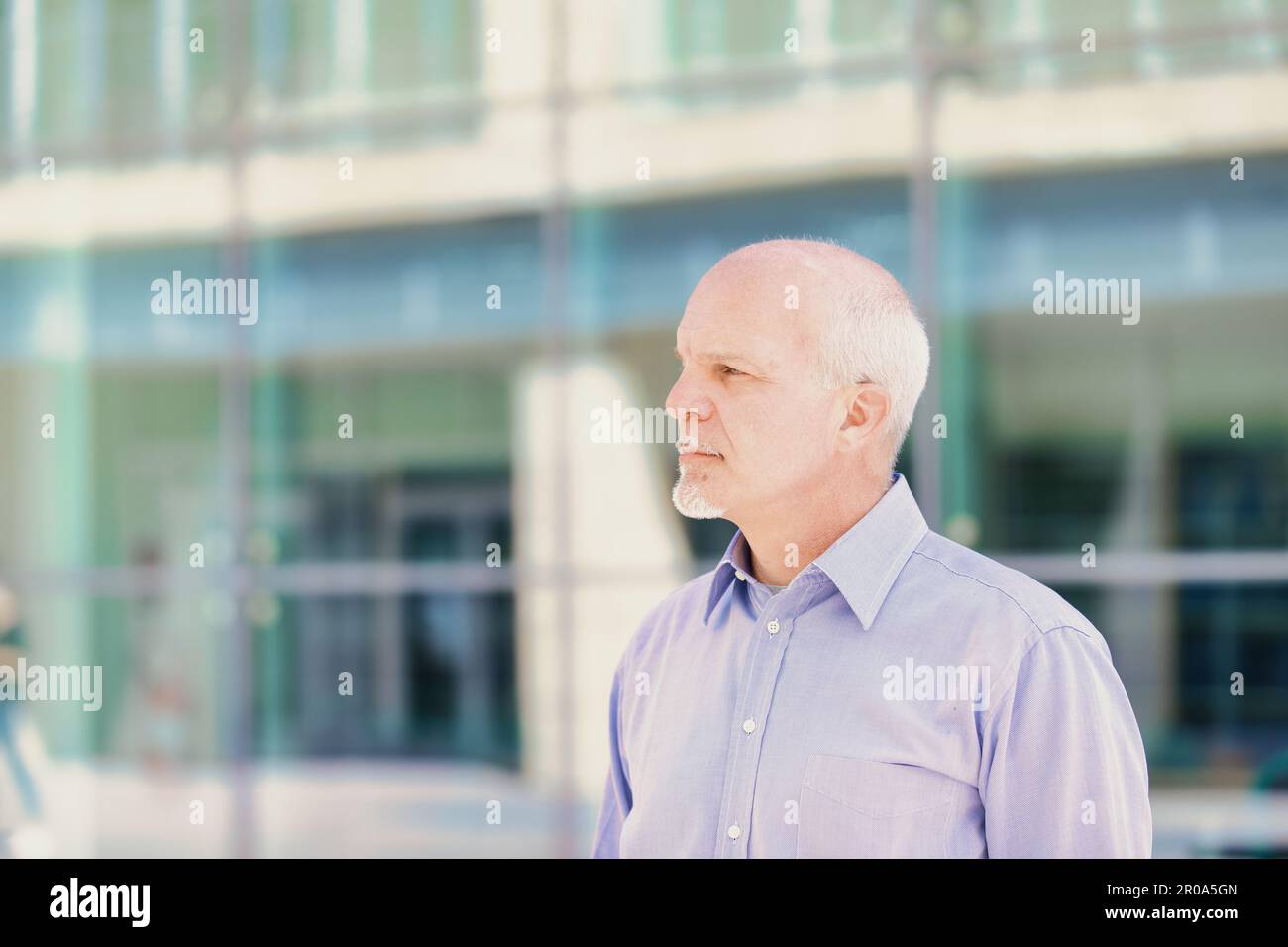 Old man outside a modern glass building, looking away and observing ...