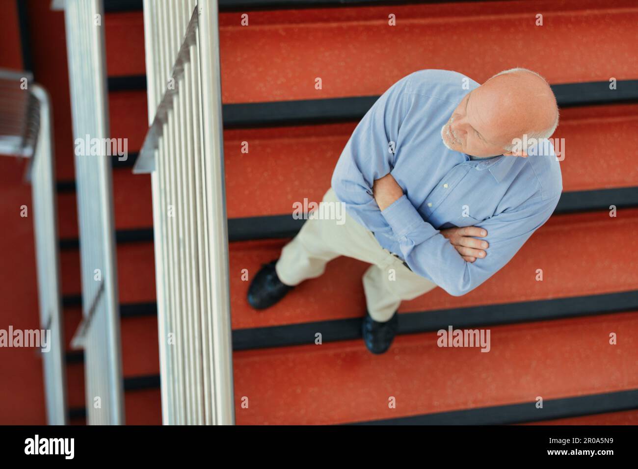 Elderly man with folded arms seen from above. He stands on a red ...