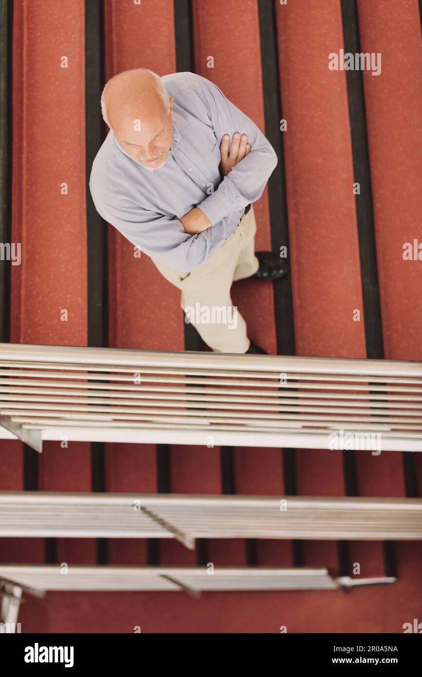 Elderly man with folded arms seen from above. He stands on a red ...