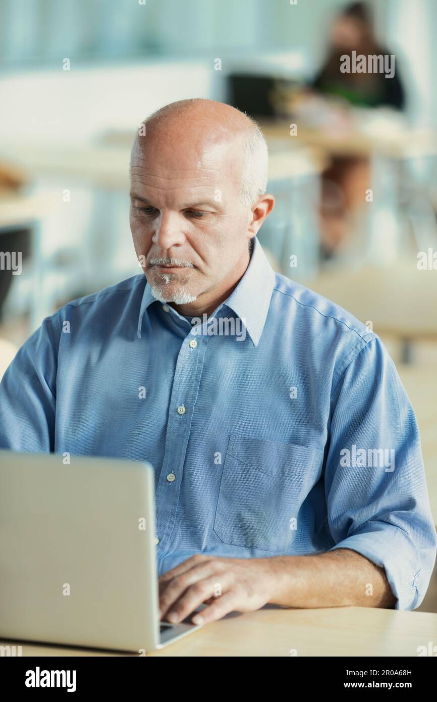 Mature person in a study hall, or in a library. Writes with a laptop ...