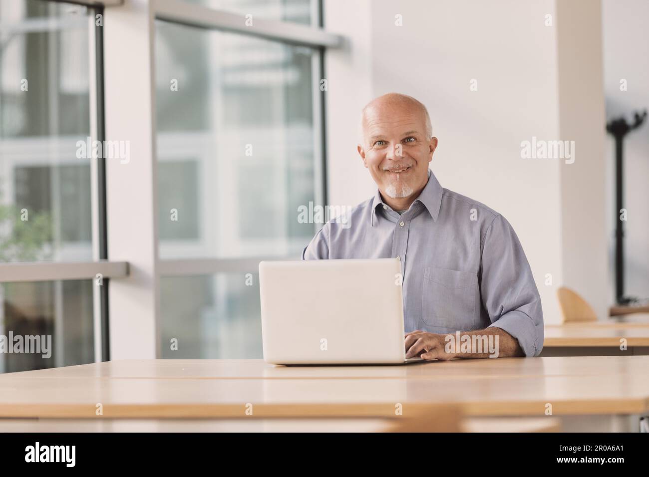 Aged man with a laptop computer in a large bright room looks at you ...