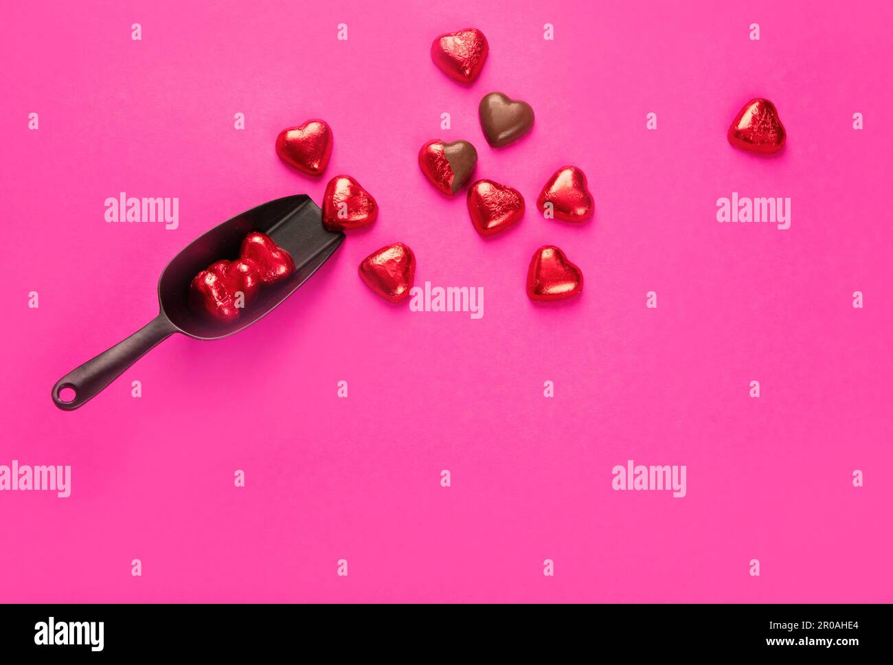 Wrapped and unwrapped heart shape chocolate candies in red foil on pink ...