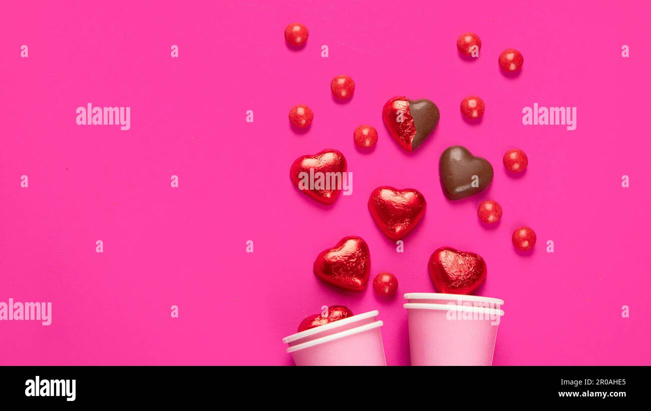 Wrapped and unwrapped heart shape chocolate candies in red foil on pink ...