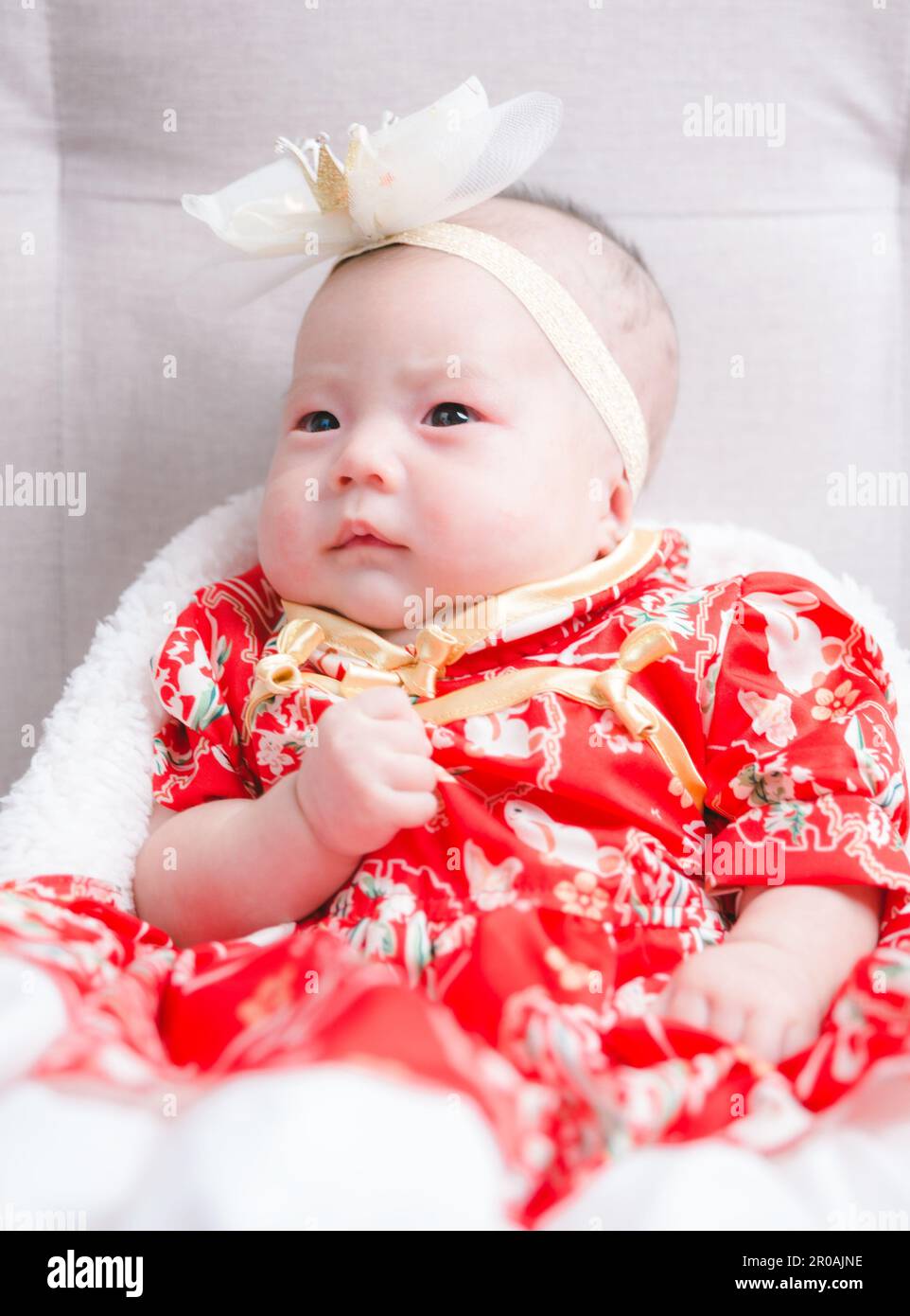 Closeup cute newborn baby in red bodysuit lying down alone on bed ...