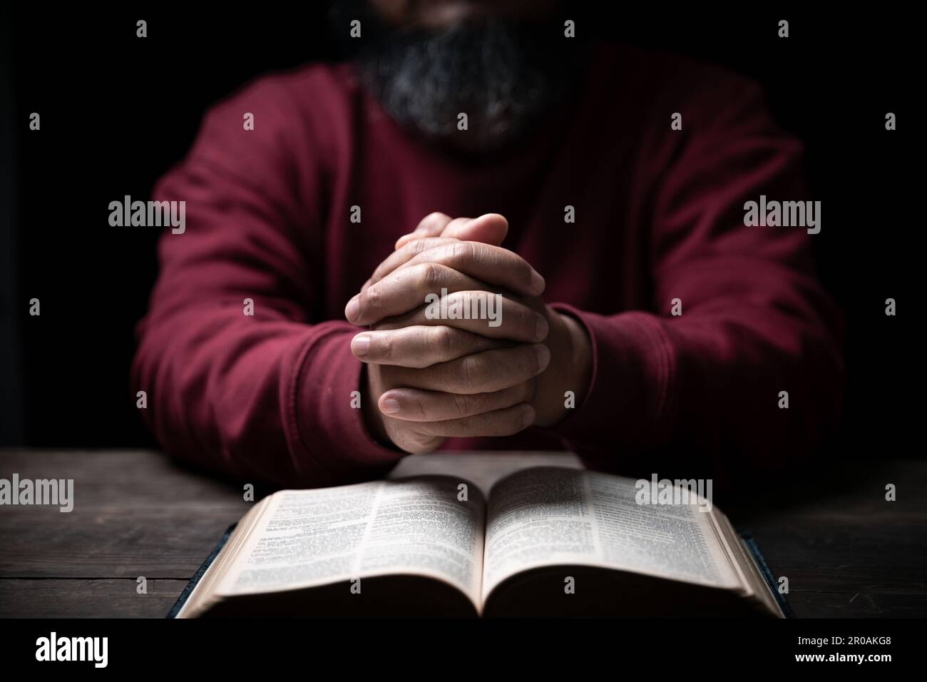 Hands folded in prayer on a Holy Bible in church concept for faith, spirituality and religion ...