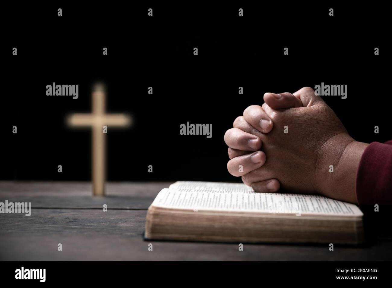 Hands folded in prayer on Holy Bible with cross in church concept for faith, spirituality and ...