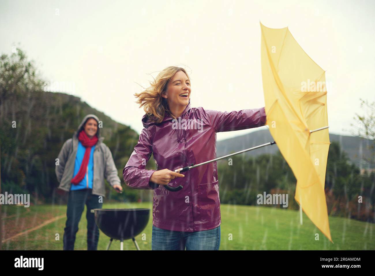 Man, woman and bbq in rain with umbrella, laugh or surprise weather ...