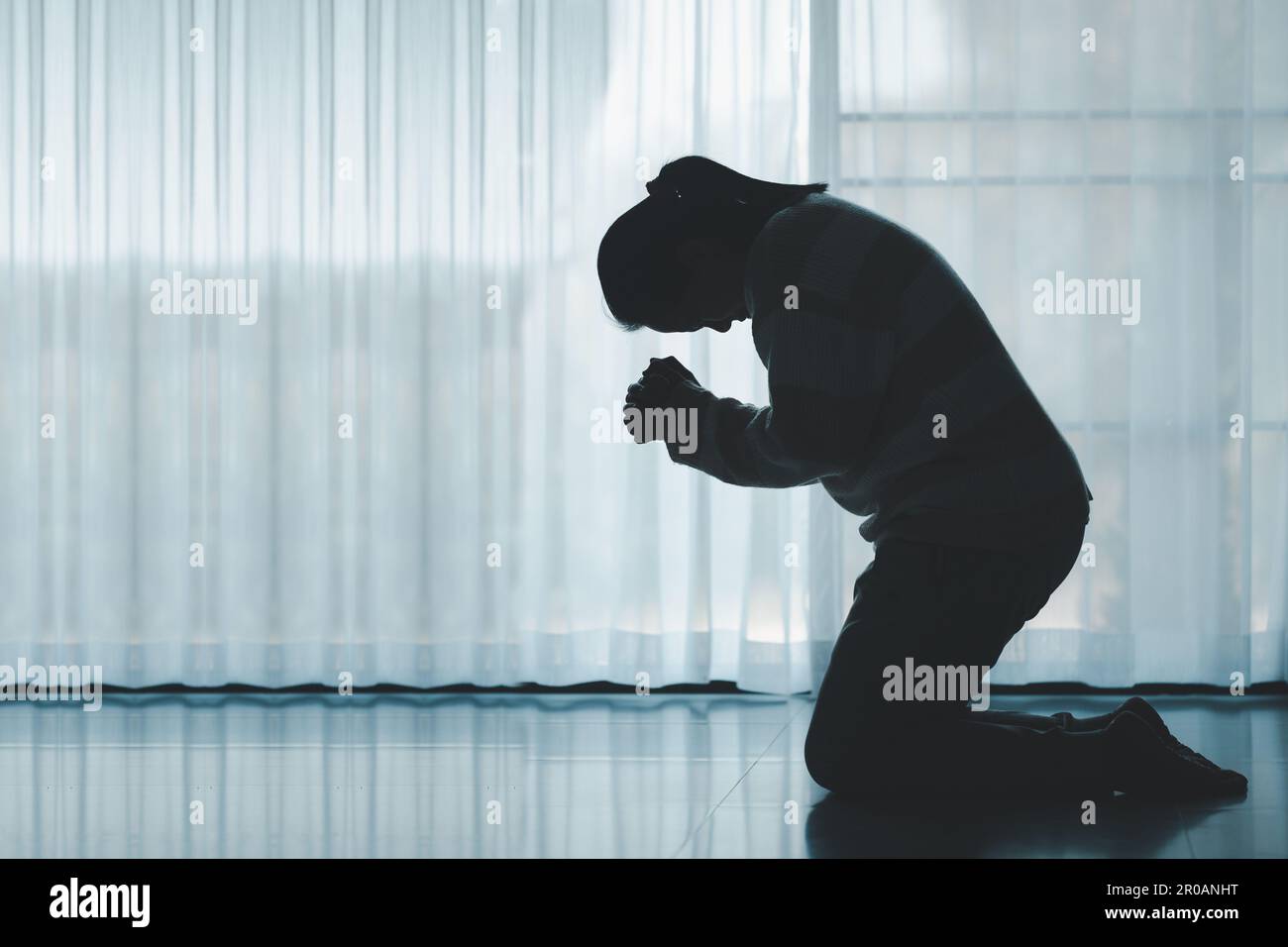 silhouette of woman kneeling and praying in modern church at sunset time. Female catholic prayer ...