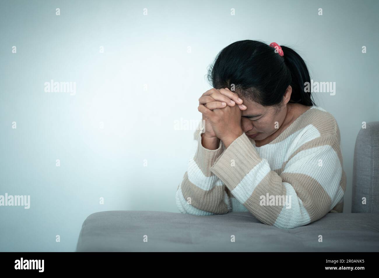 woman kneeling and praying in modern house at sunset time. Female catholic prayer worship to God ...
