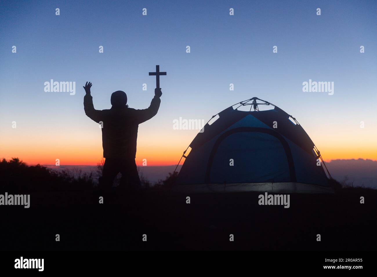 Silhouette of man kneeling down praying for worship God at sky background. Christians pray to ...