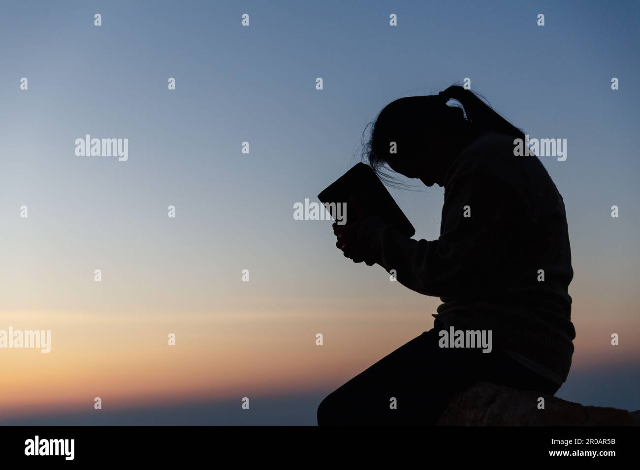 Silhouette of woman kneeling down praying for worship God at sky background. Christians pray to ...