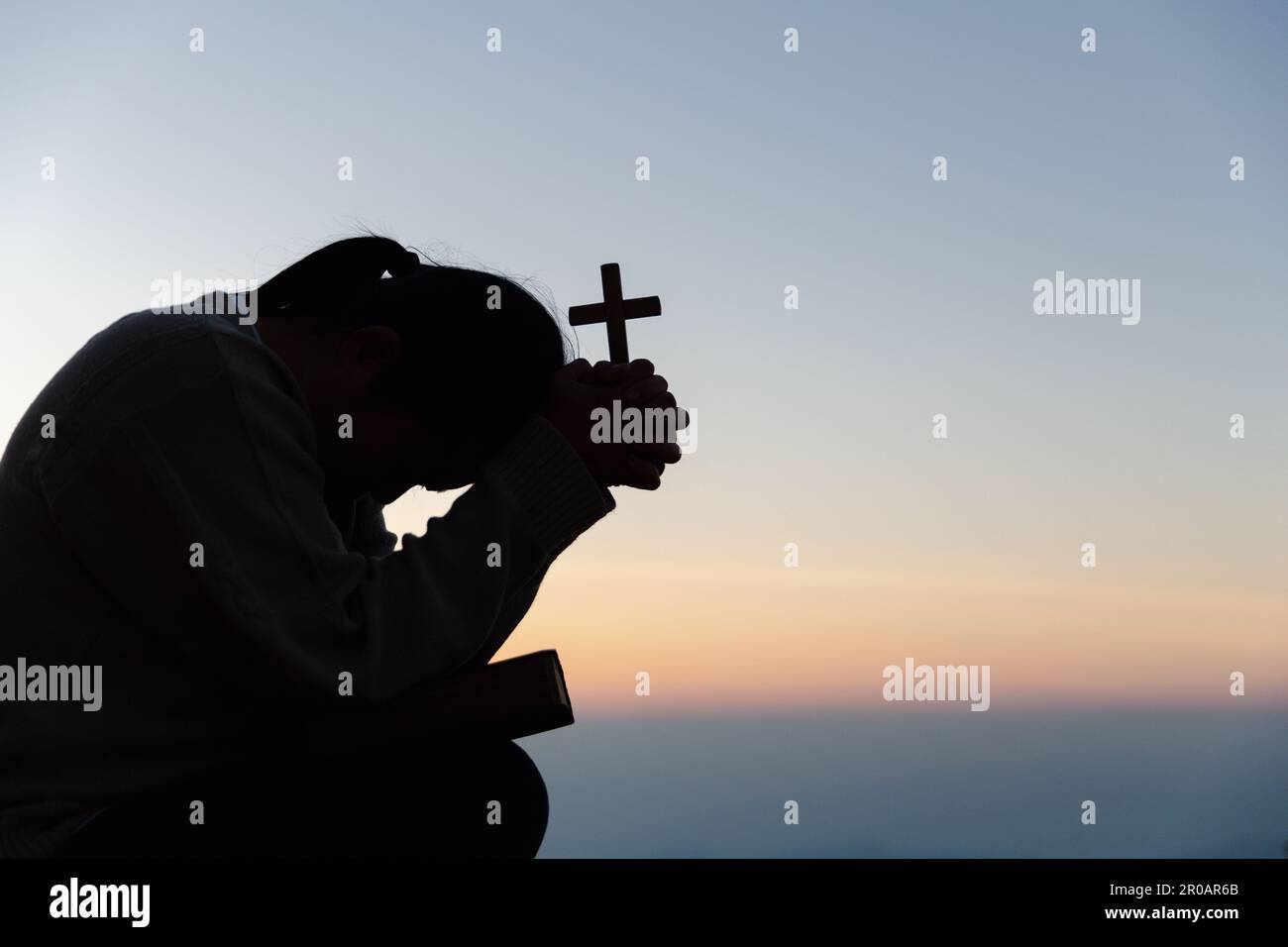 Silhouette of woman kneeling down praying for worship God at sky background. Christians pray to ...