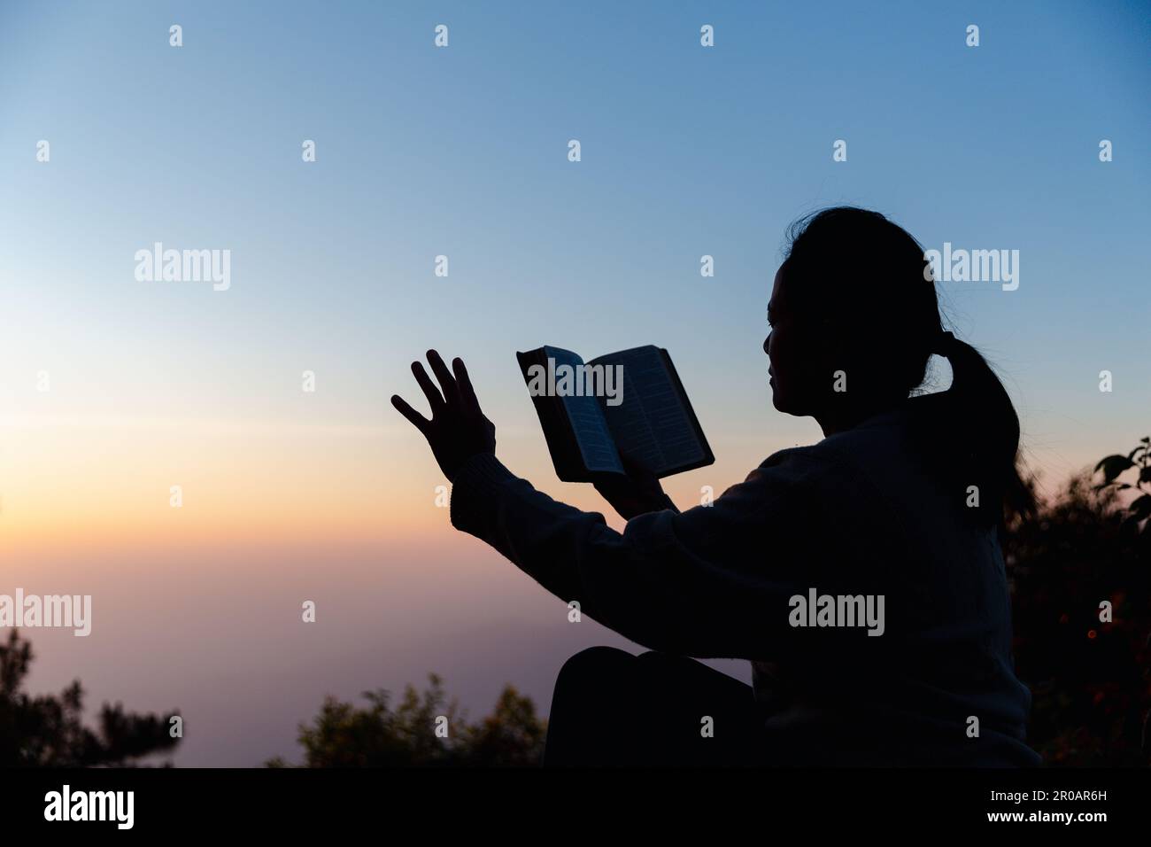 Silhouette of woman kneeling down praying for worship God at sky background. Christians pray to ...