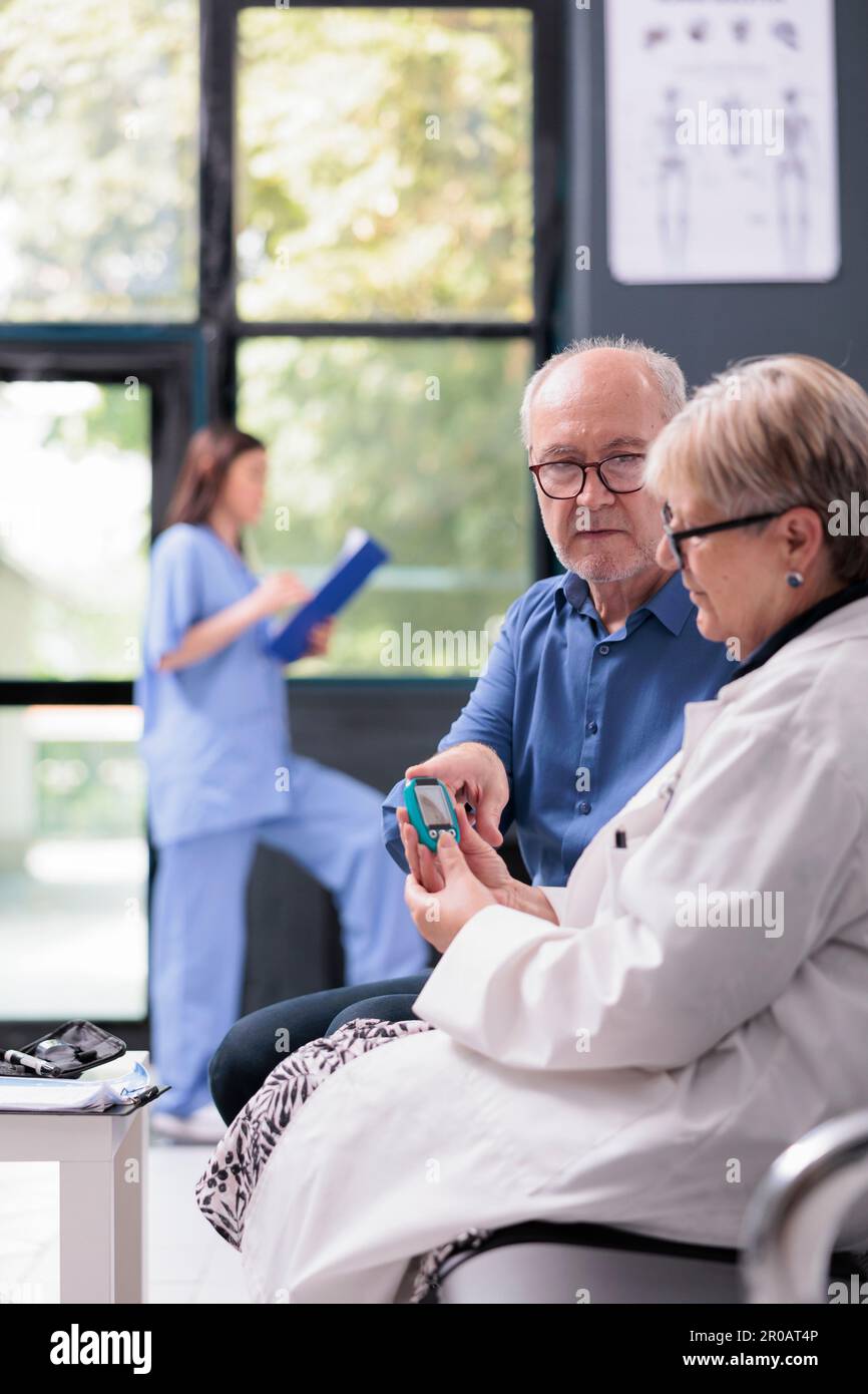 Elderly physician taking patient insulin level test using glucometer in ...