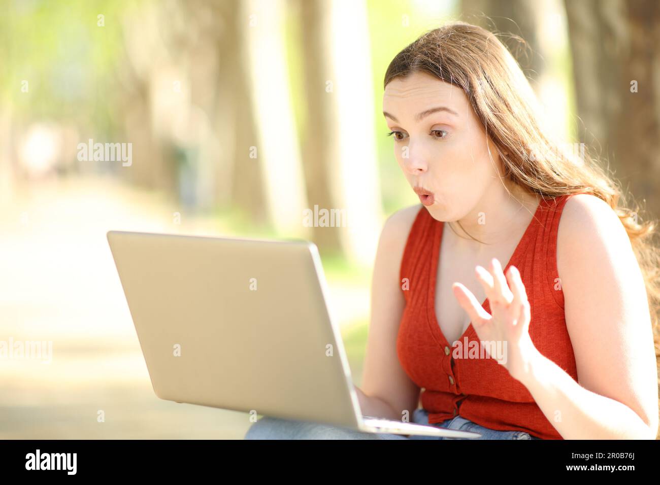 Surprised woman checking laptop content sitting alone in a park Stock ...