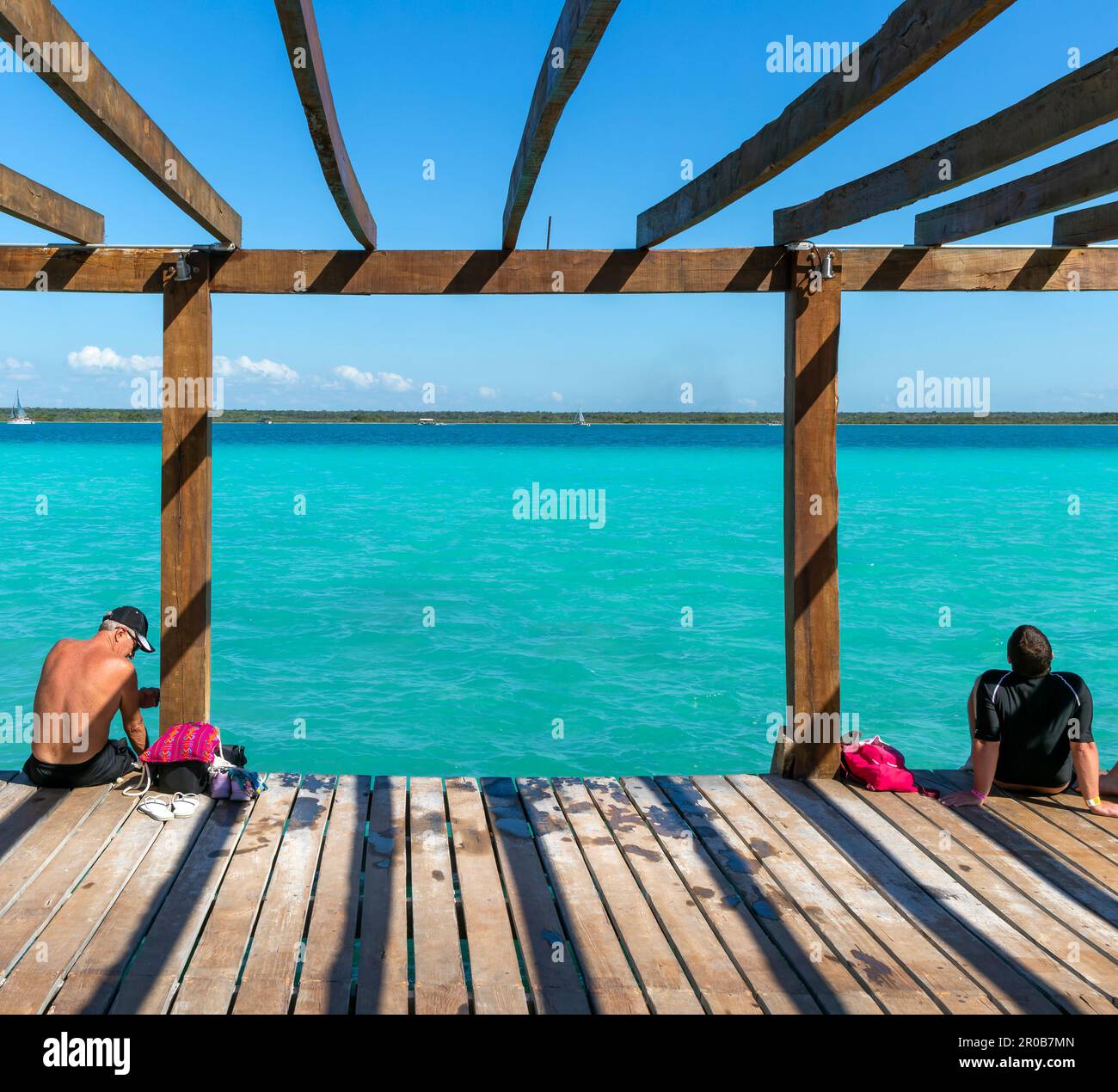 People sitting on woooden jetty pier by waterside, Lake Bacalar ...