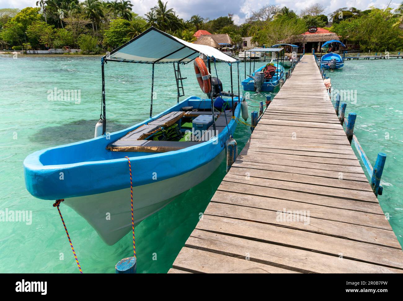 Boats moored on wooden jetty leading to land on Lake Bacalar, Bacalar ...