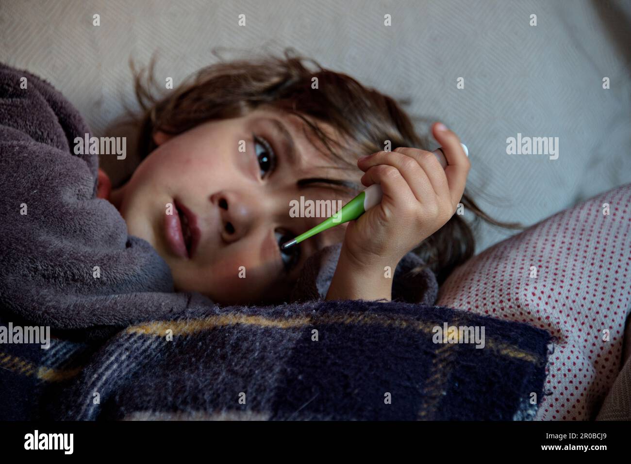 Cold child lying on the bed looking at the thermometer Stock Photo - Alamy
