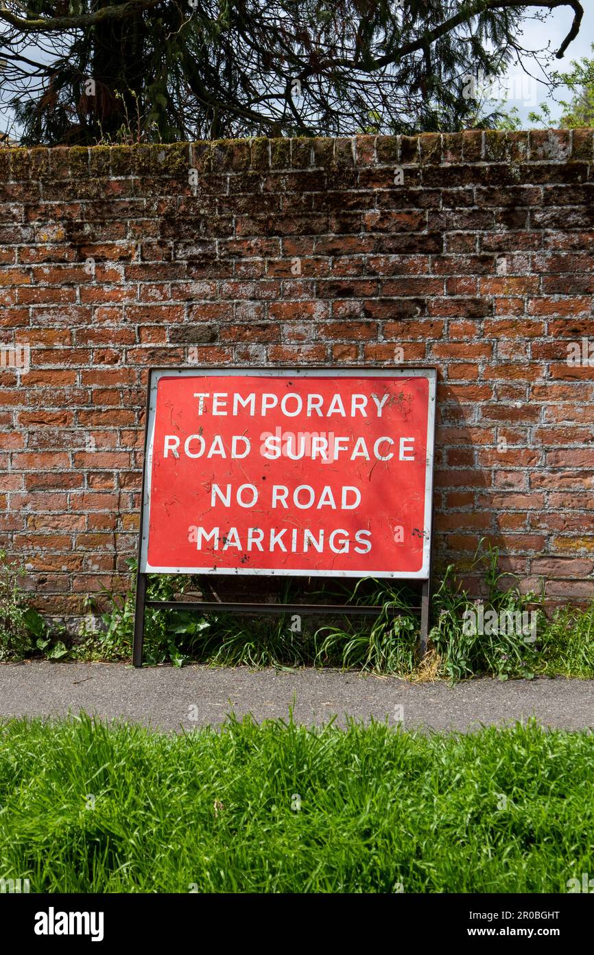 A misplaced warning road sign propped up on the pavement by a wall in ...