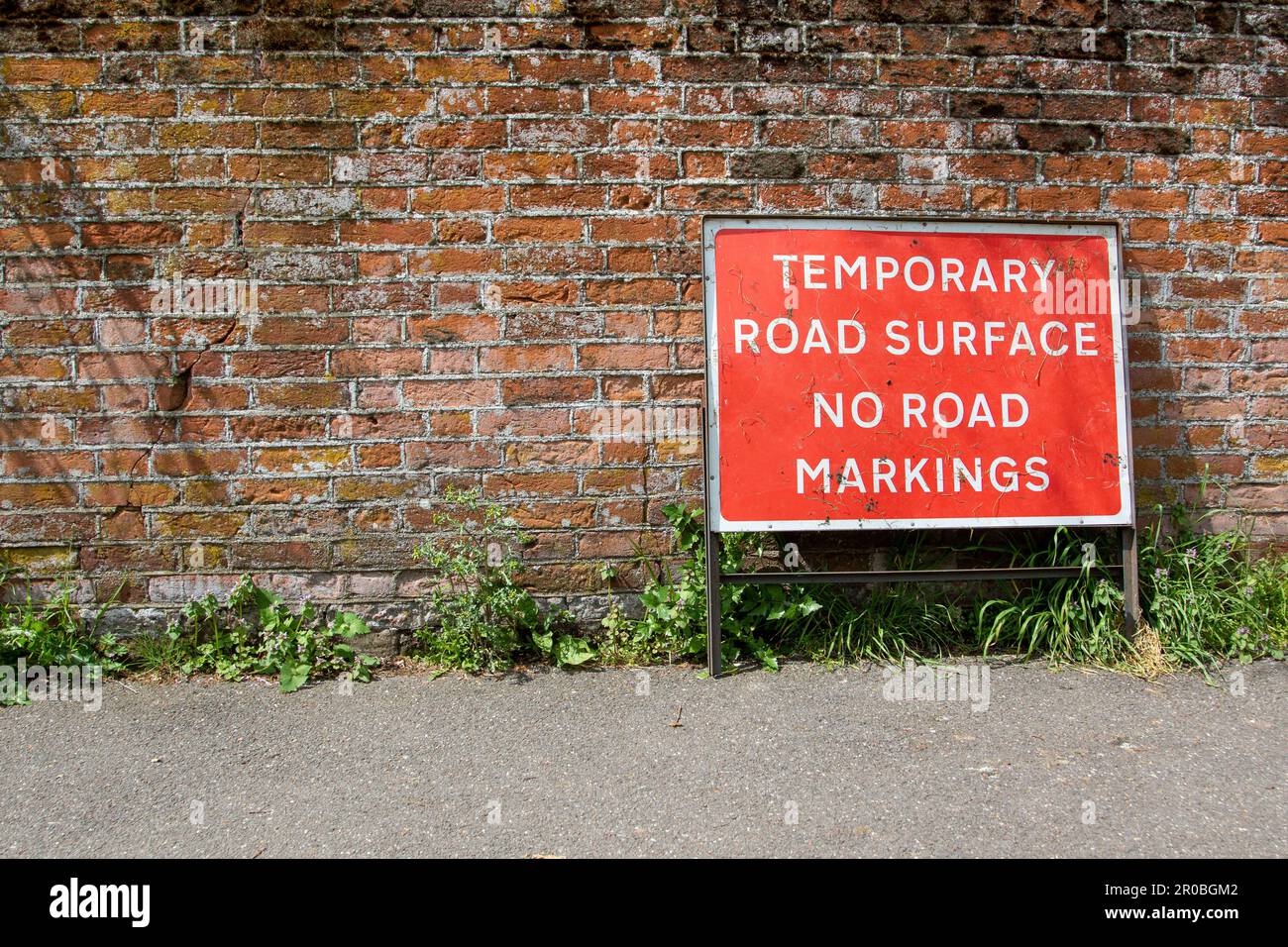 A misplaced warning road sign propped up on the pavement by a wall in ...