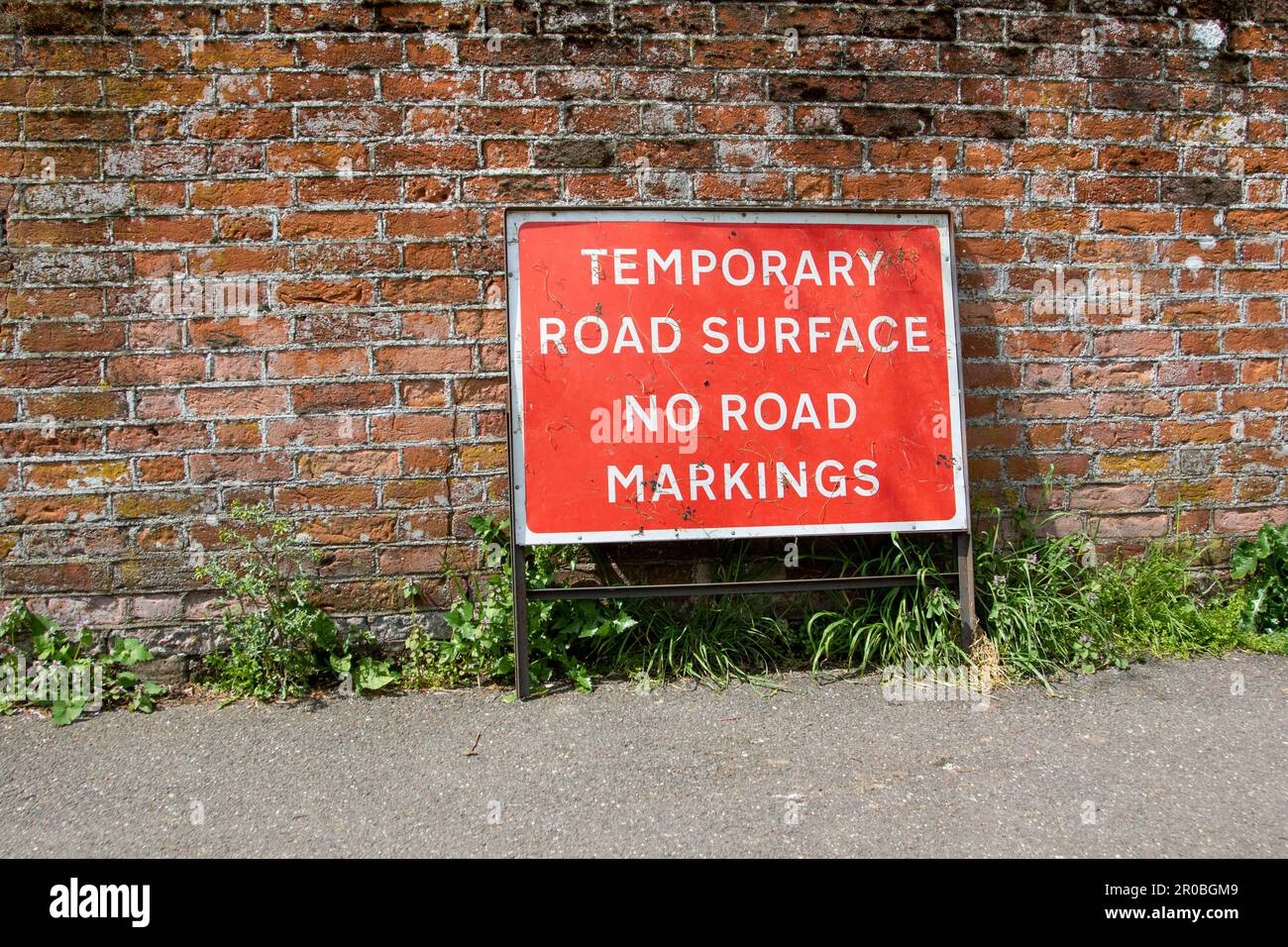 A misplaced warning road sign propped up on the pavement by a wall in ...
