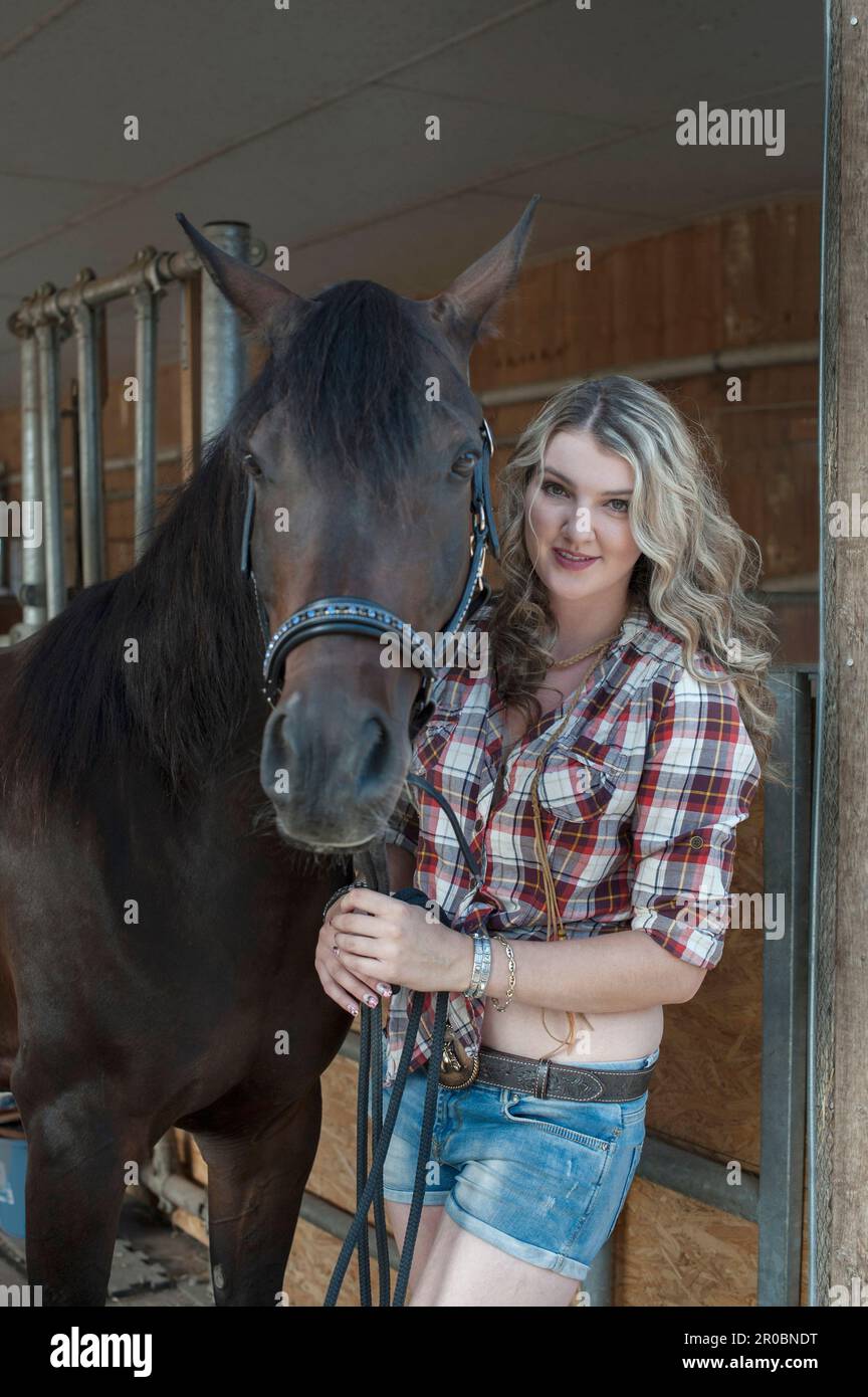 Young woman standing with her brown horse in stable, Bavaria, Germany ...