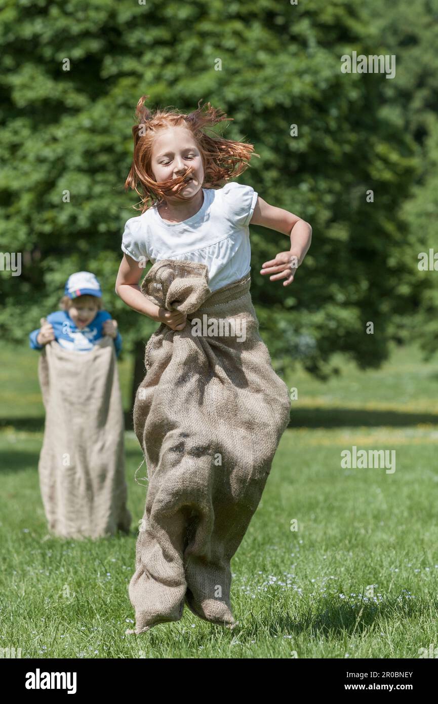 Two girls jumping in sack race in a field, Munich, Bavaria, Germany ...