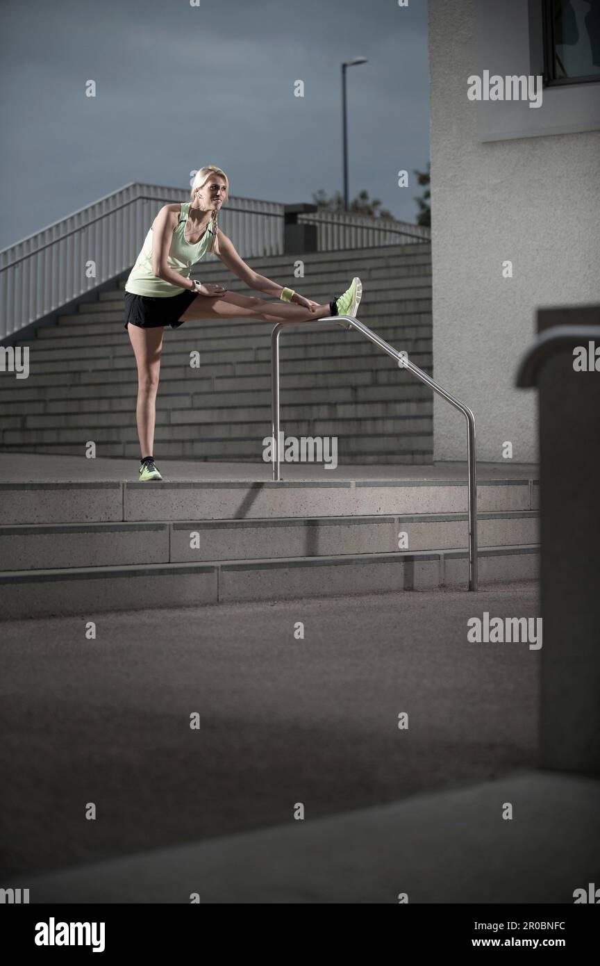 Mid adult woman stretching her leg on railing during dawn, Bavaria ...