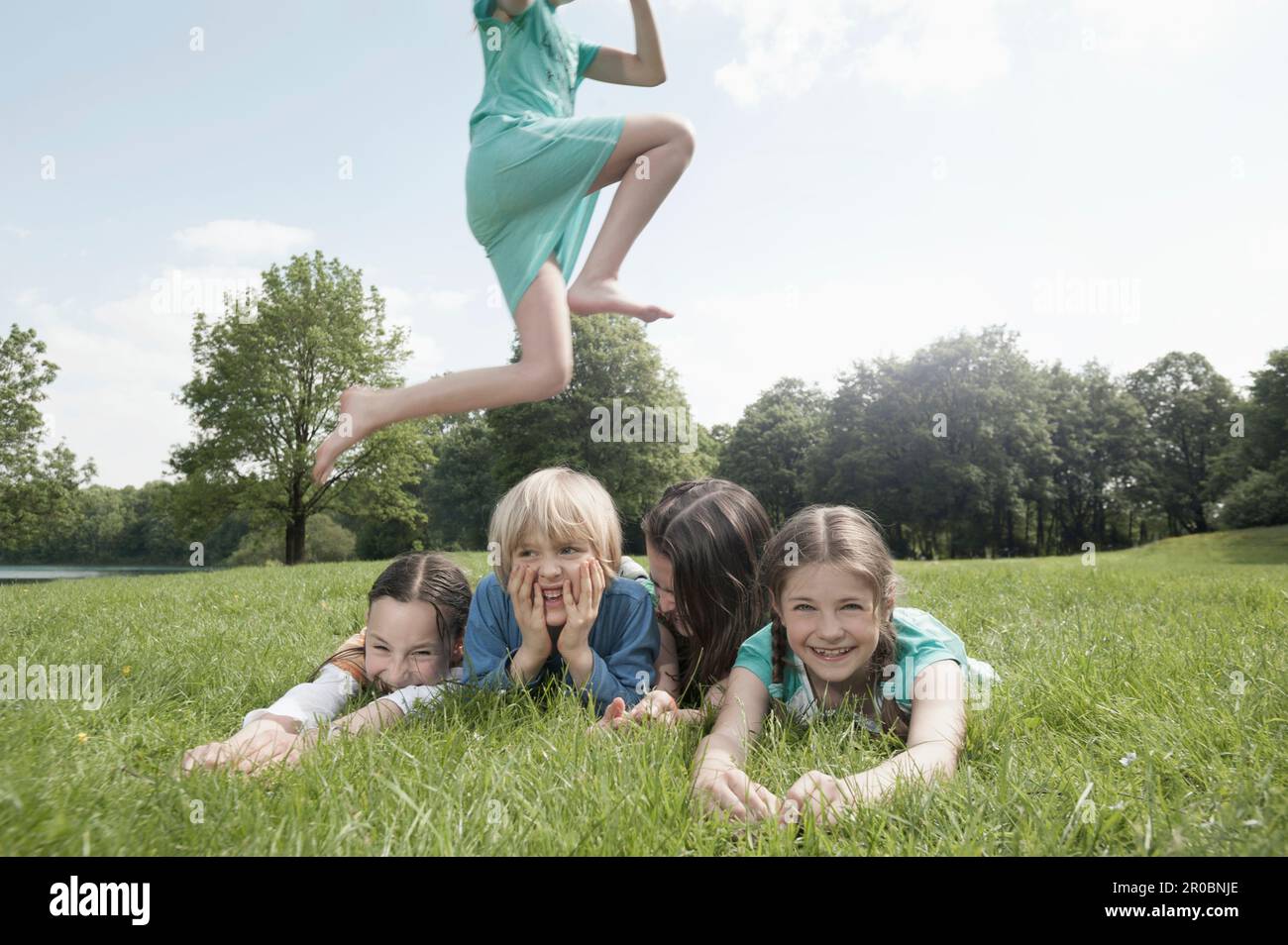 Girl jumping over her friends lying on grass in a park, Munich, Bavaria ...