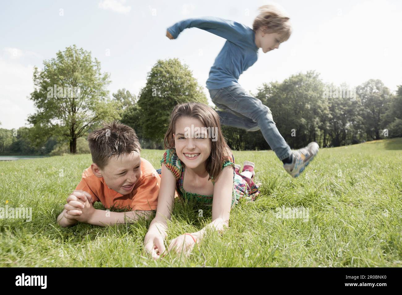 Boy jumping over his friends lying on grass in a park, Munich, Bavaria ...