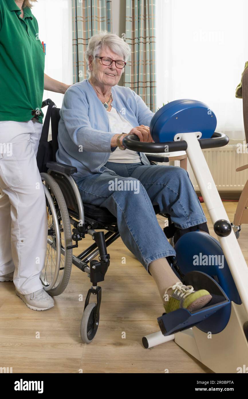 Nurse with senior woman on wheelchair exercising on exercise bike in ...