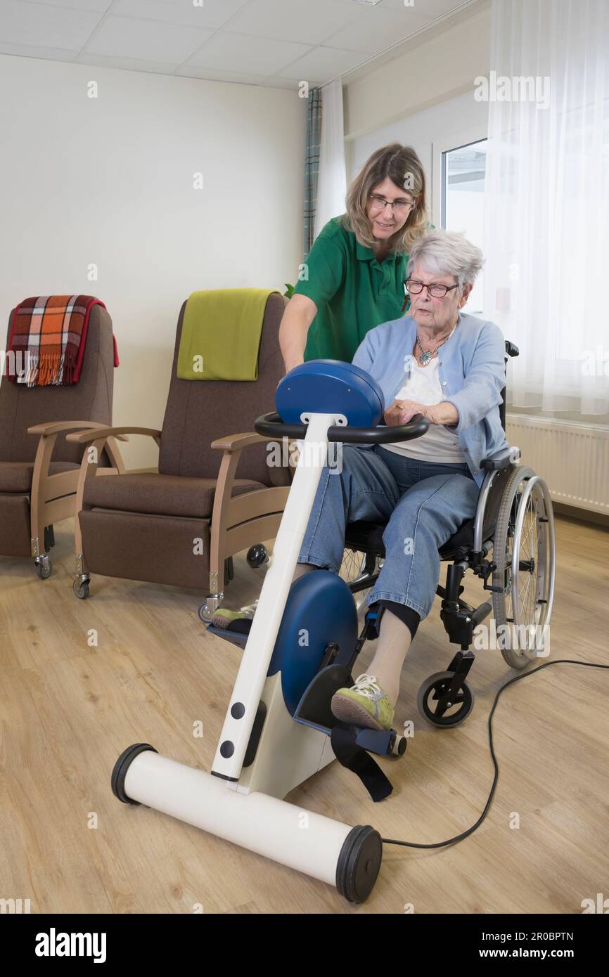 Nurse with senior woman on wheelchair exercising on exercise bike in ...