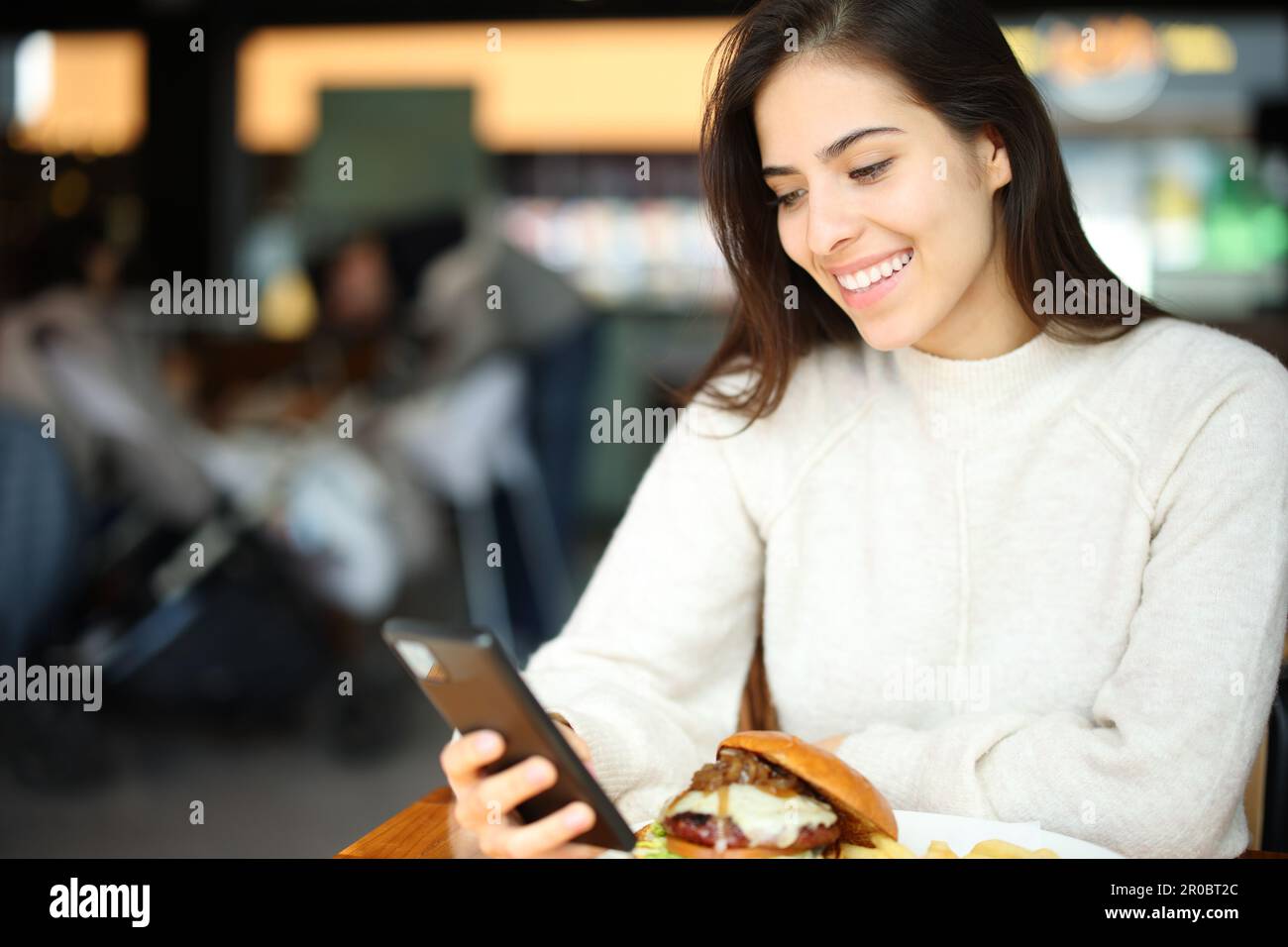 Customer checking smart phone sitting in a restaurant Stock Photo - Alamy