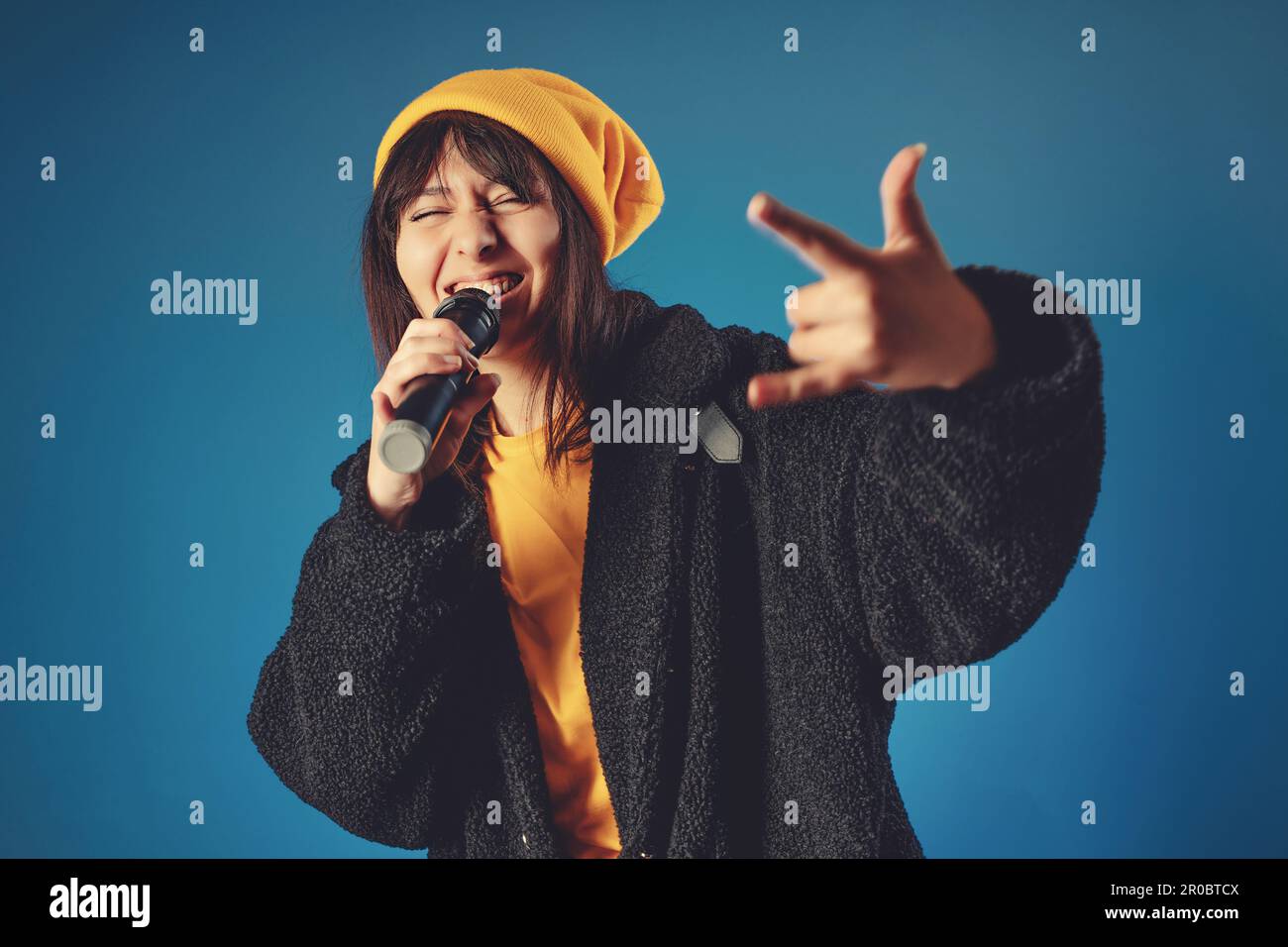 Stylish woman in yellow hat and shirt singing into a microphone, making ...