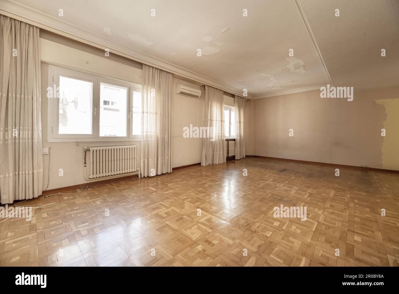 A large empty room in a house with parquet floors, several windows with ...