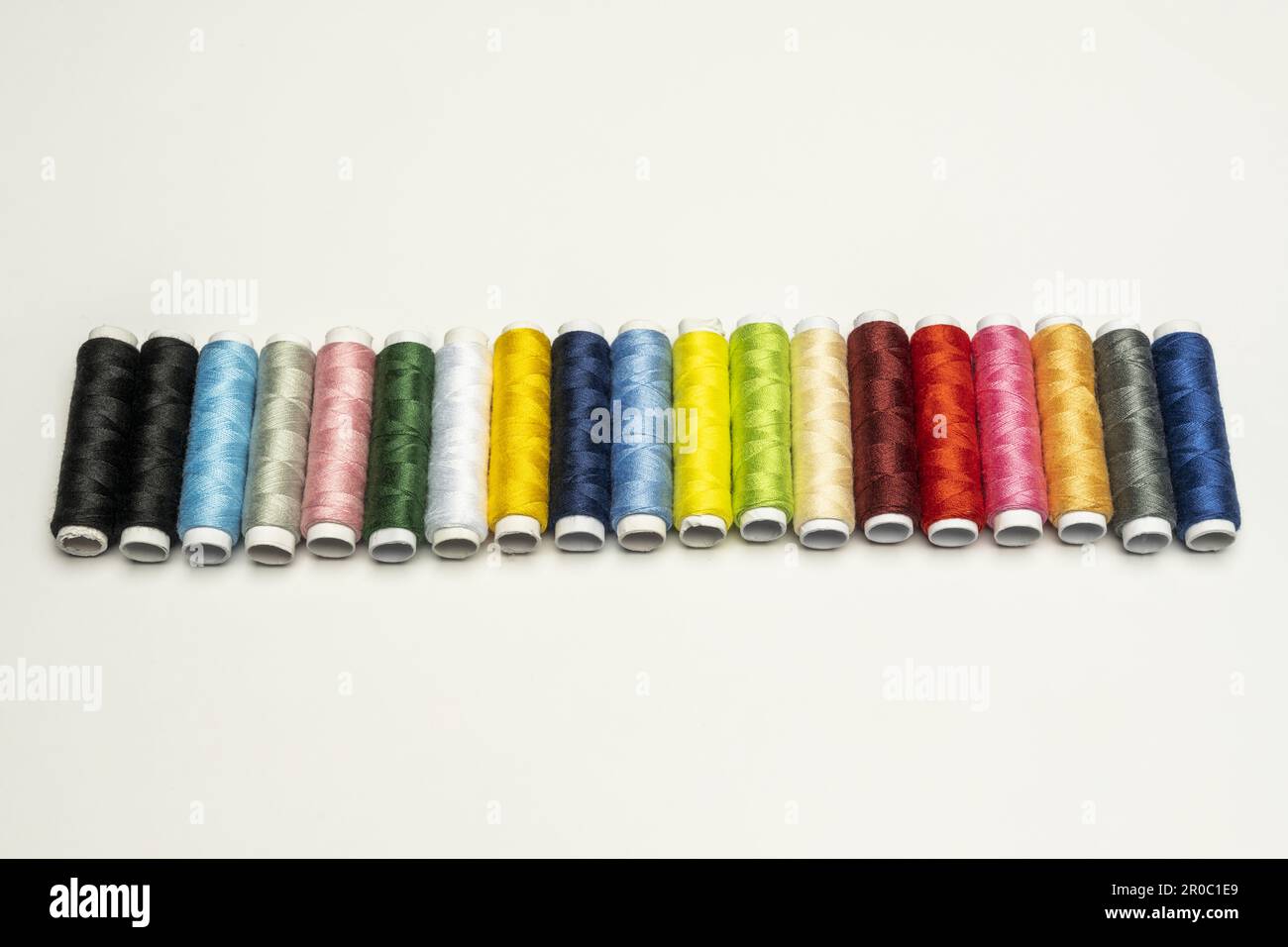 A strip of new spools of colored sewing thread on a plain white ...