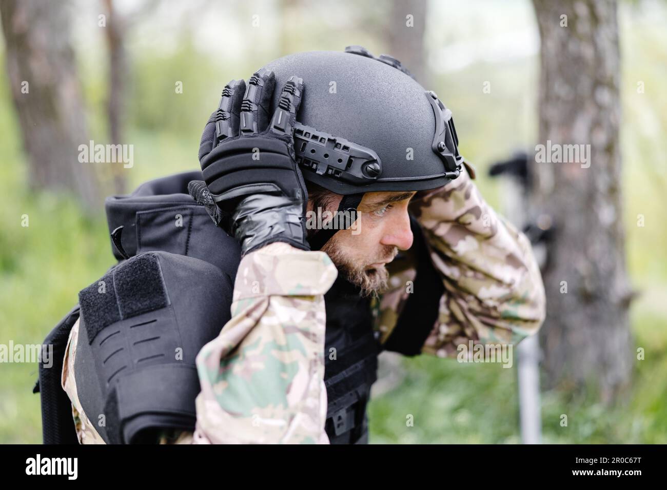 A man in a military uniform and a bulletproof vest works in the forest ...