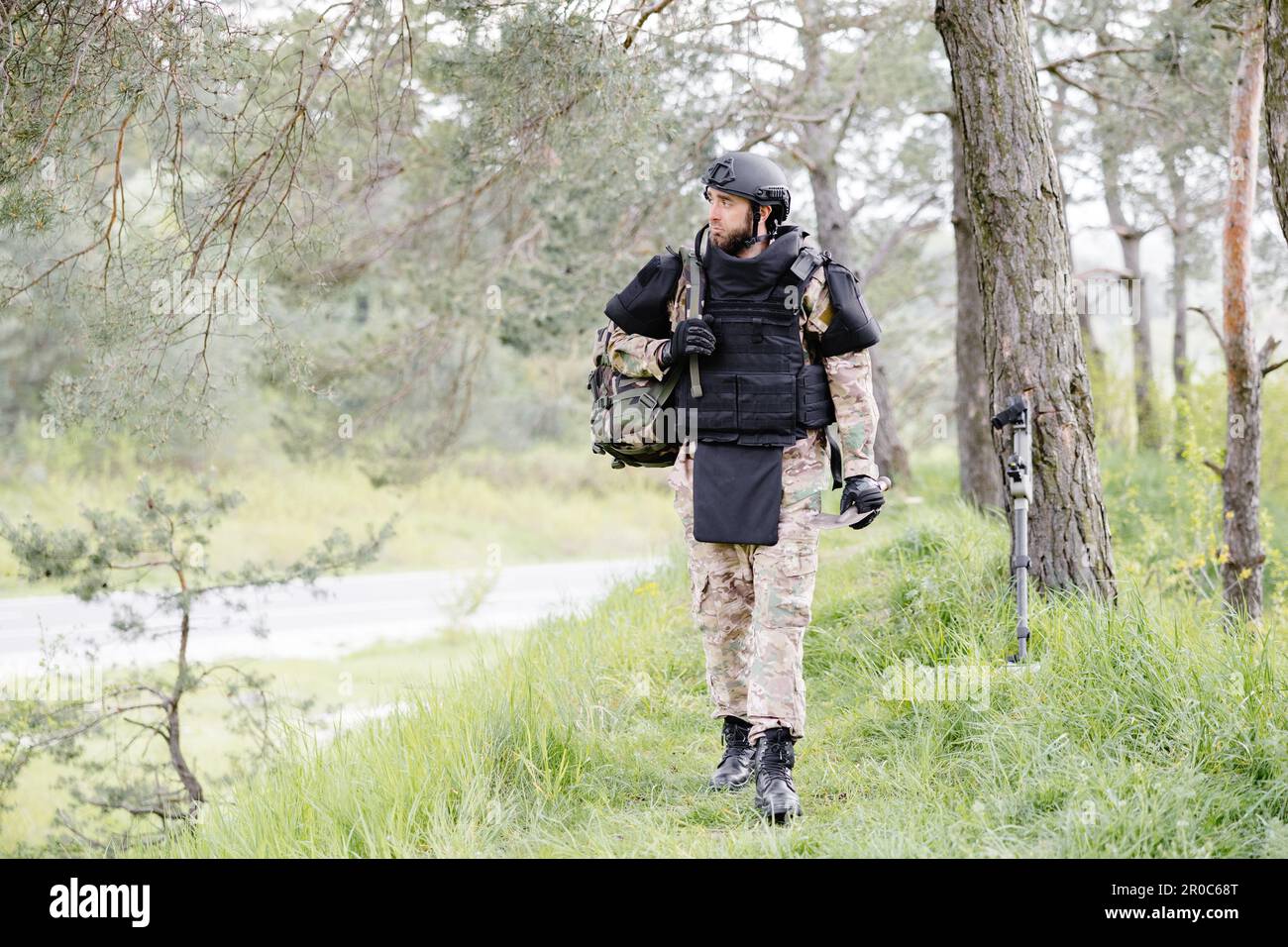 Young soldier in uniforms and tactical vest works in the forest and ...