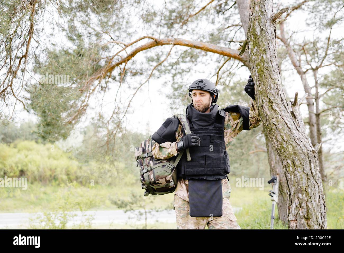 Young soldier in uniforms and tactical vest works in the forest and ...