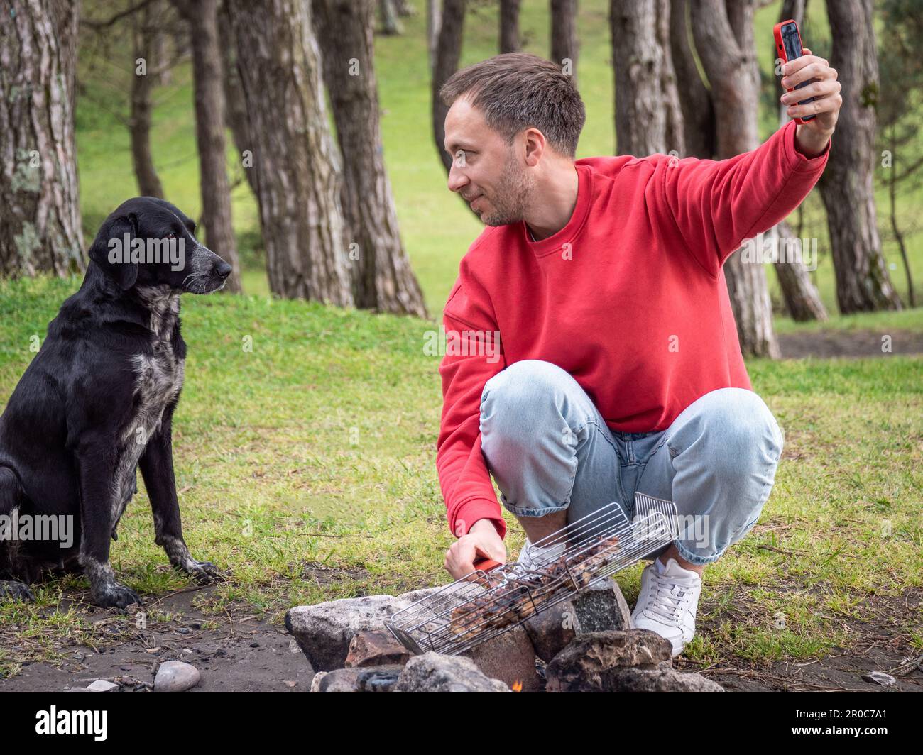 Young man take selfie with dog and roast meat on fire, picnic with pet ...