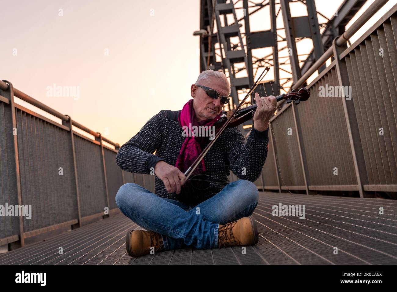 attractive middle aged musician man playing an electric violin outdoors ...