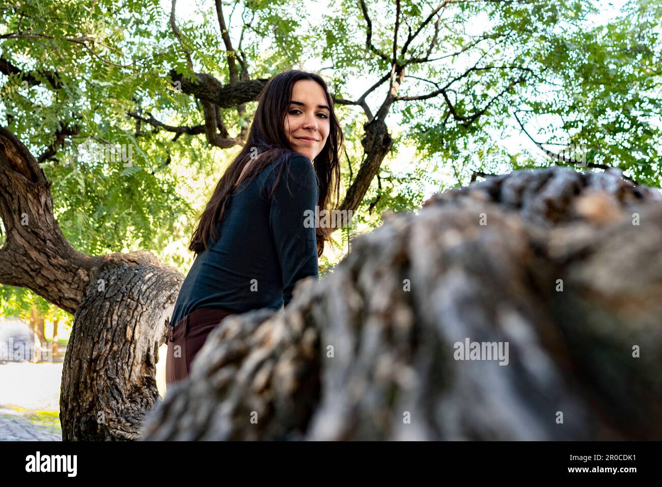 A woman sitting on a tree branch posing and looking at the camera in a ...
