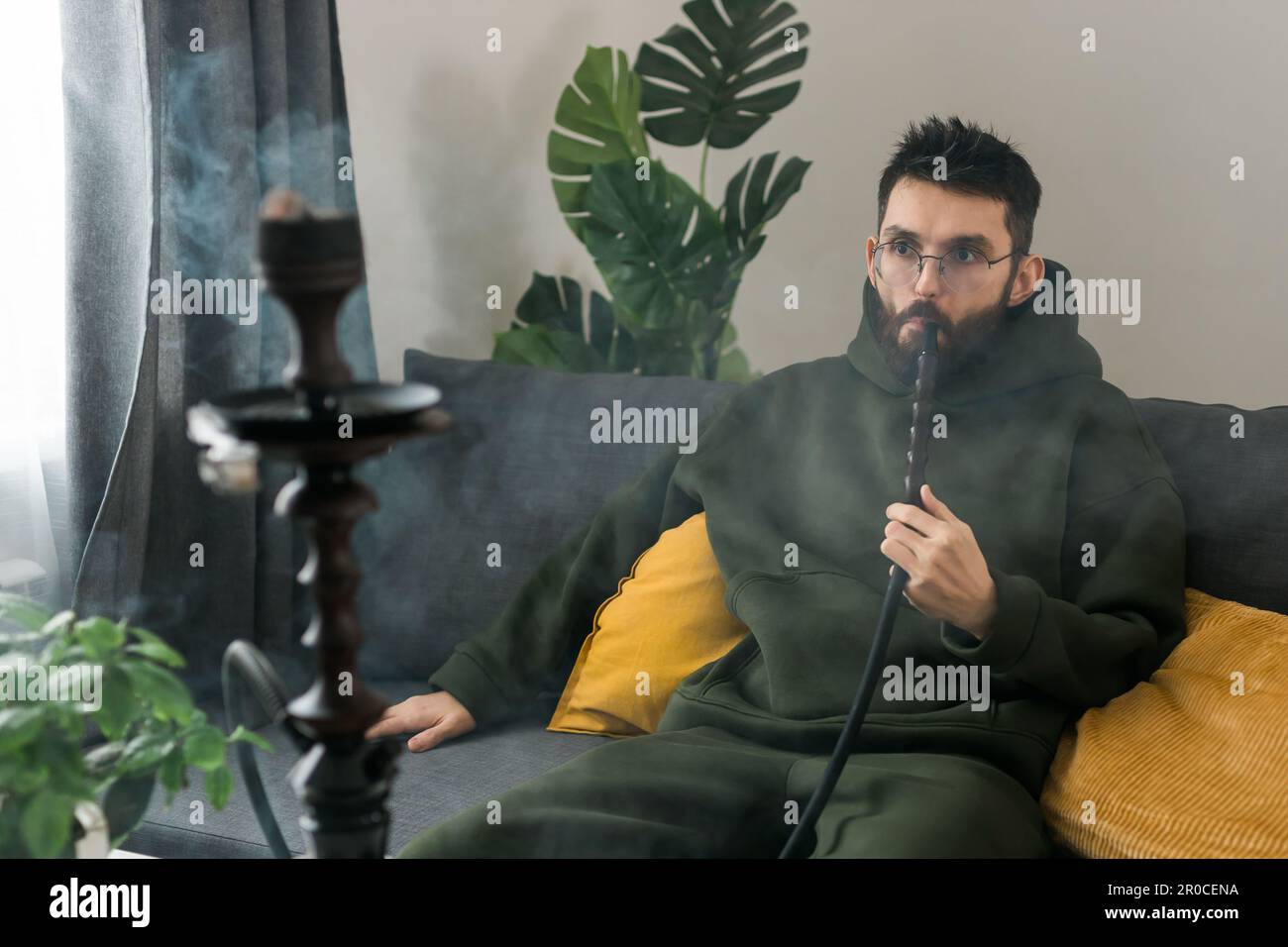 Bearded millennial or gen z man smoking hookah while relaxing on sofa ...