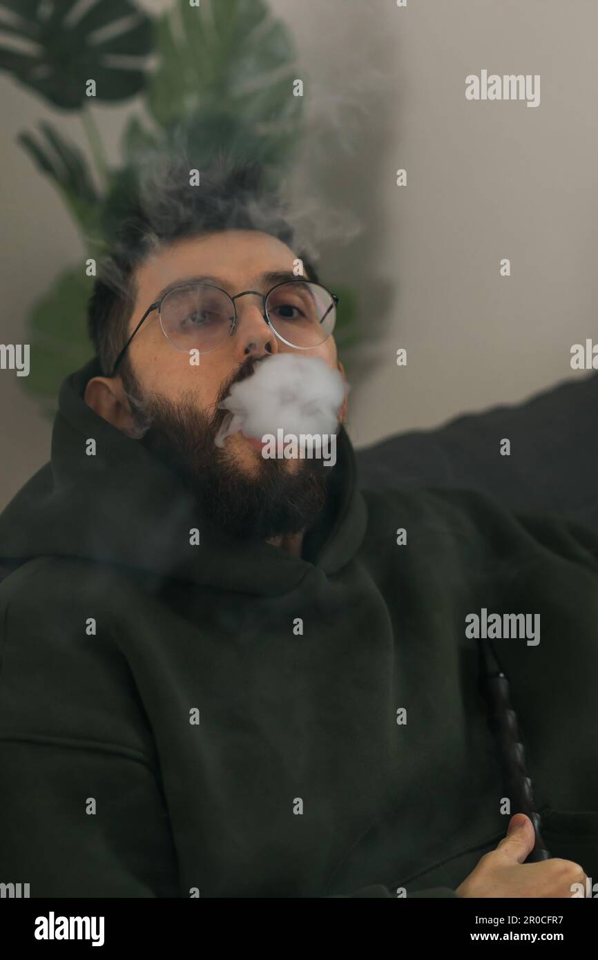 Bearded millennial or gen z man smoking hookah while relaxing on sofa ...
