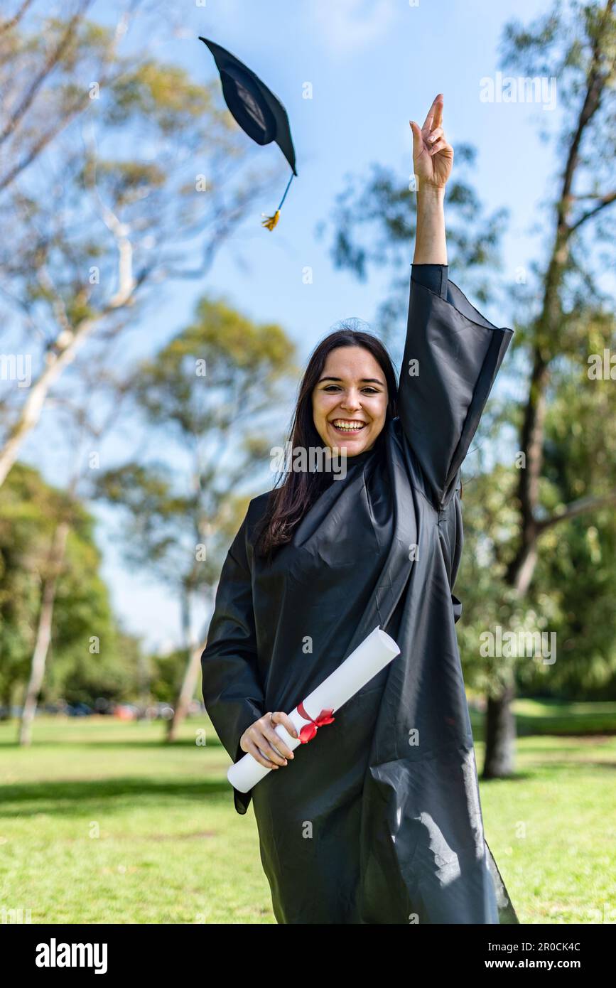Happy caucasian graduated girl in a black gown throwing the mortarboard ...