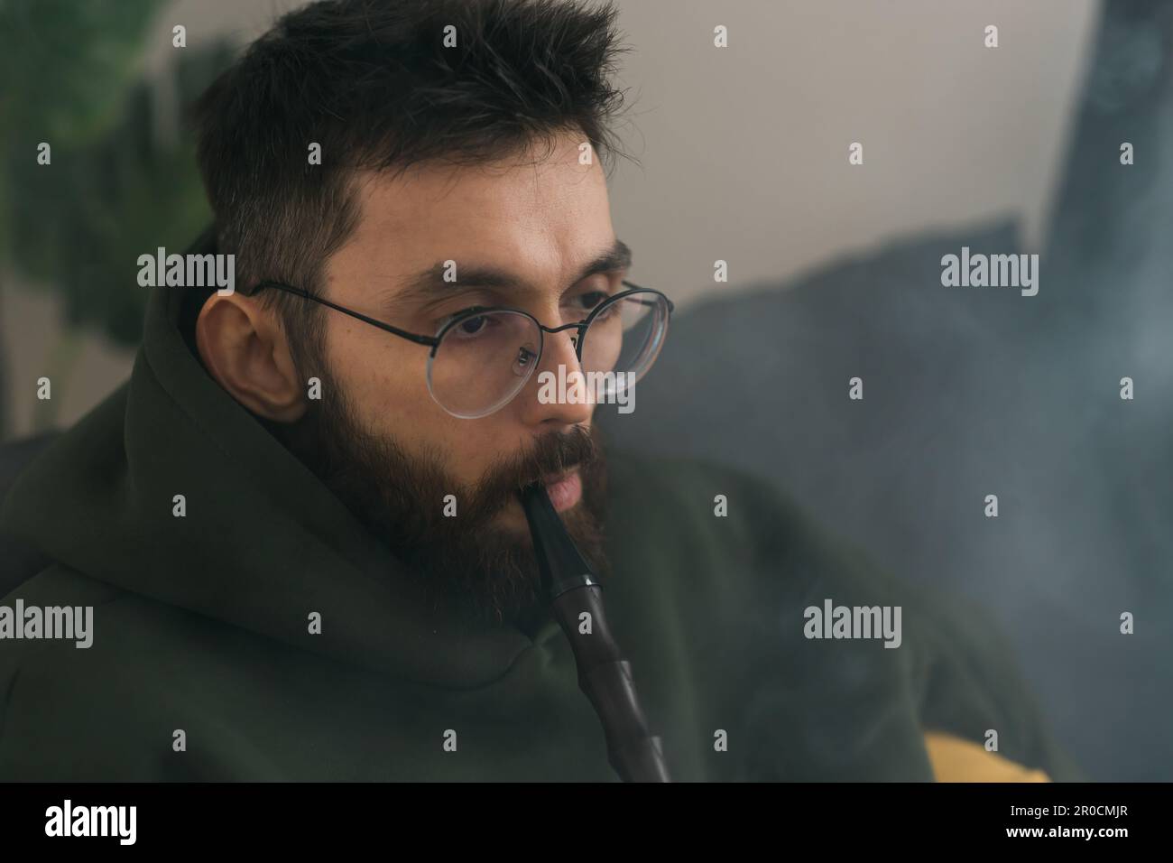 Bearded millennial or gen z man smoking hookah while relaxing on sofa ...