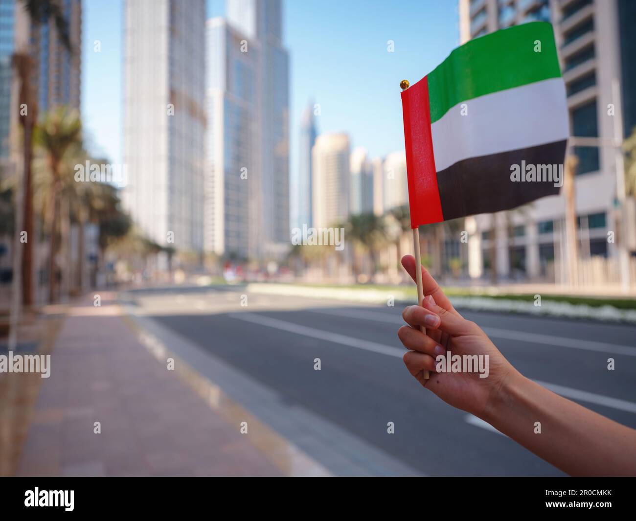 Close up of a female hand holding tiny flag of UAE against Dubai ...