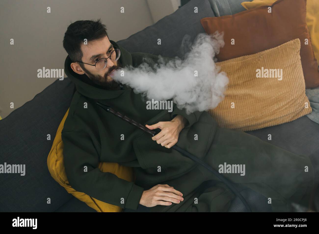 Bearded millennial or gen z man smoking hookah while relaxing on sofa ...