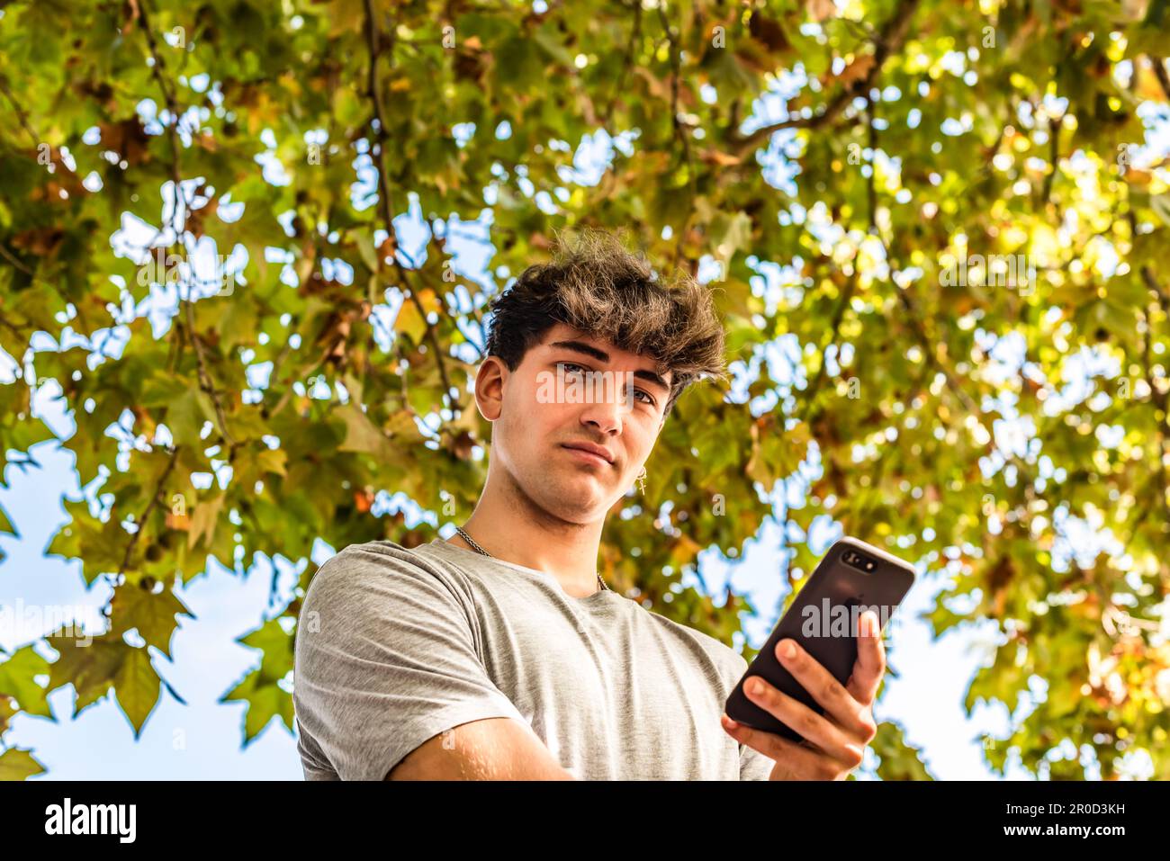 Low angle of a young man holding his smartphone, serious, looking at ...