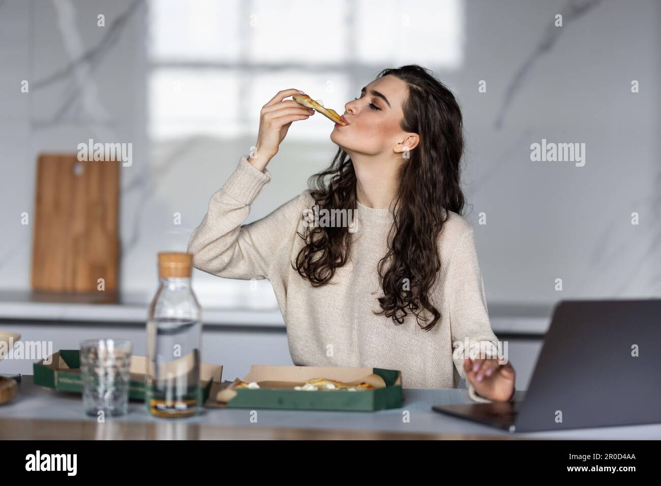 Overworked woman taking a break and eating pizza, working from home on ...